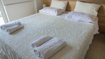 Cama bem arrumada com lençóis e toalhas brancos, cabeceira de madeira e parede lisa.