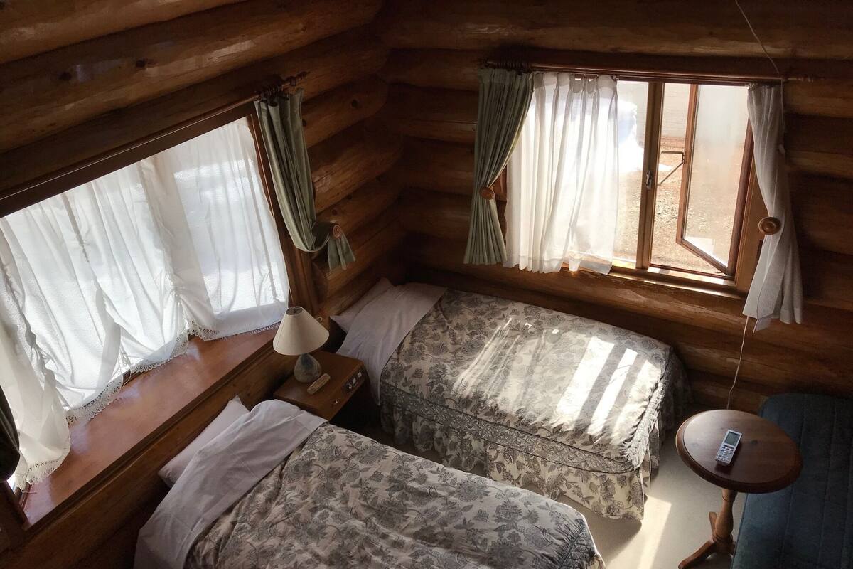 Um quarto de cabana aconchegante com duas camas, uma mesa pequena e uma janela com cortinas.