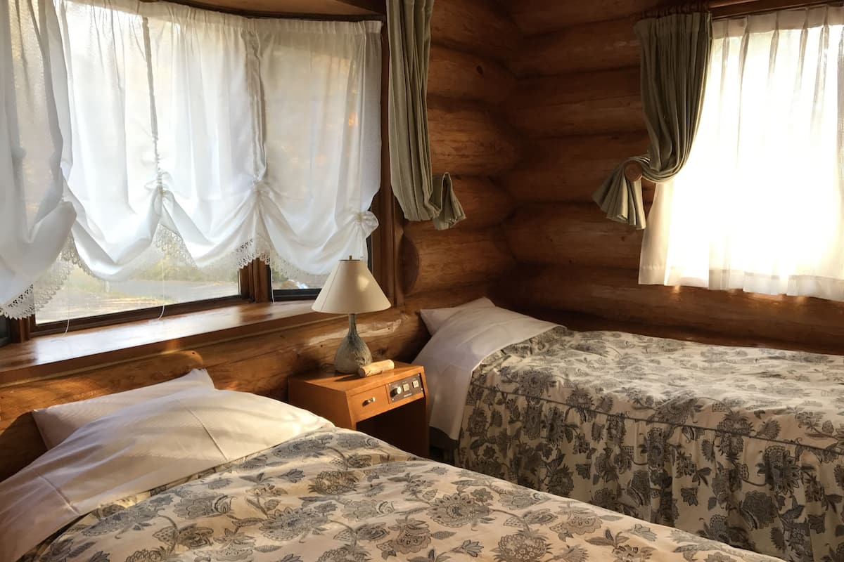 Quarto de cabana aconchegante com duas camas, uma mesinha de cabeceira e uma luminária.