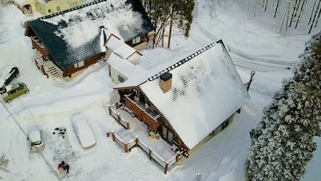Uma cabana coberta de neve com fachada de madeira, varanda coberta e chaminé visível.