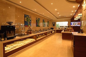 Uma área de buffet com estação de café, diversas opções de comida e obras de arte nas paredes.