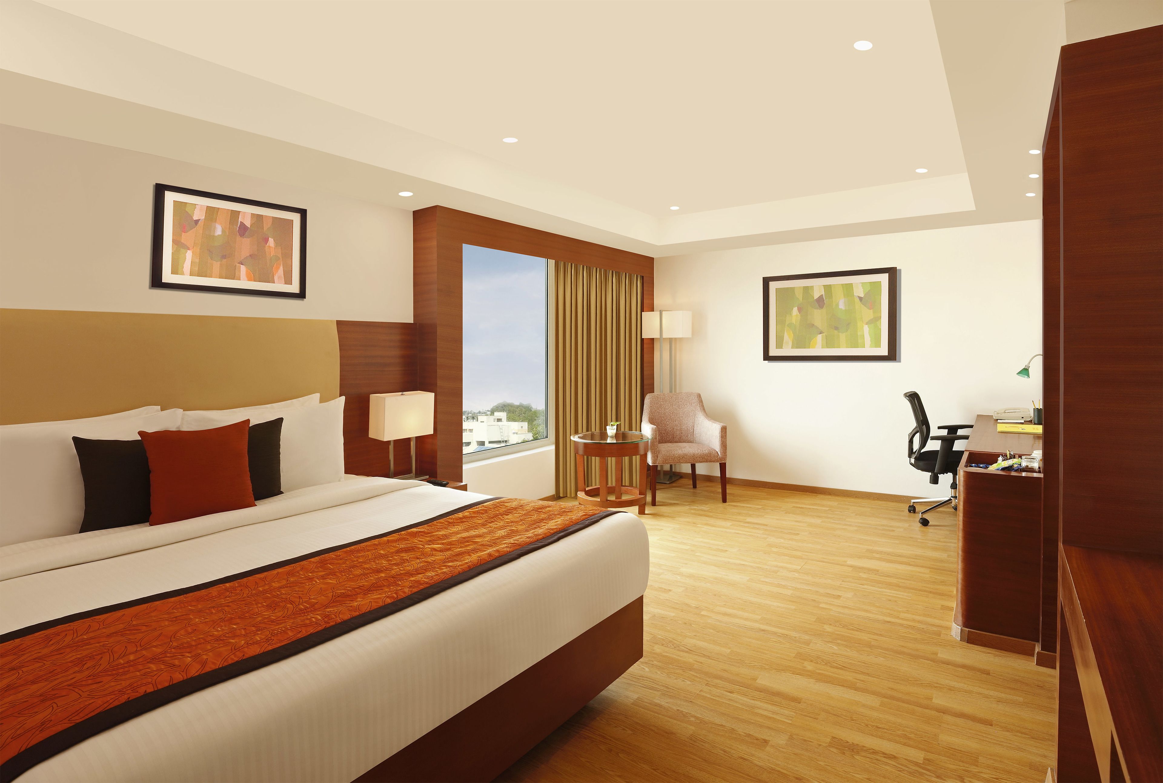 Quarto de hotel com uma cama grande, uma escrivaninha, uma cadeira e uma janela com vista.