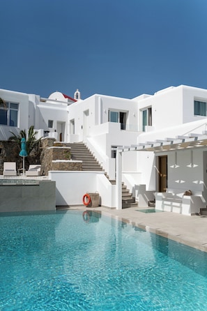 Um edifício moderno branco com piscina, degraus de pedra e céu azul límpido.