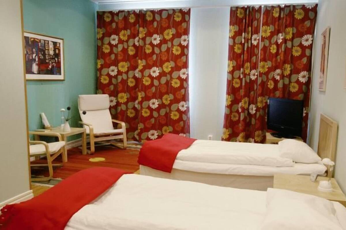 Quarto de hotel com duas camas, uma televisão, uma cadeira e uma mesinha.