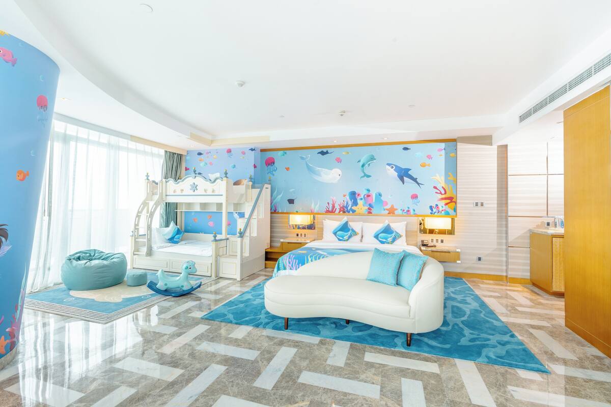Quarto para crianças com cama beliche, um sofá branco e um mural com tema oceânico.