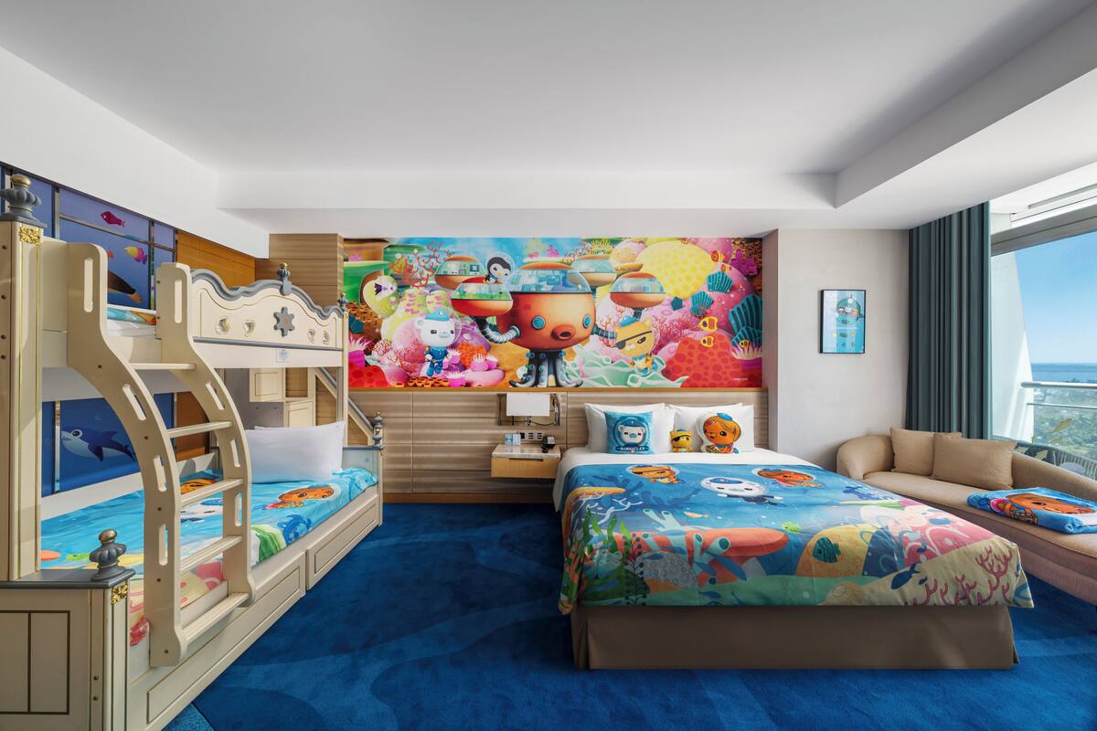 Quarto infantil com beliches, um grande mural, um sofá e vista para o mar.