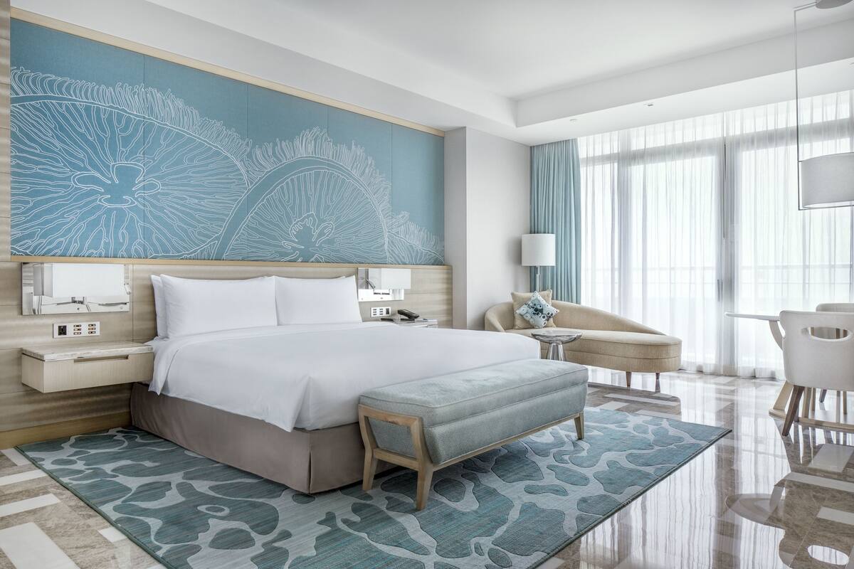 Quarto de hotel moderno com uma cama grande, área de estar e vista para a cidade.