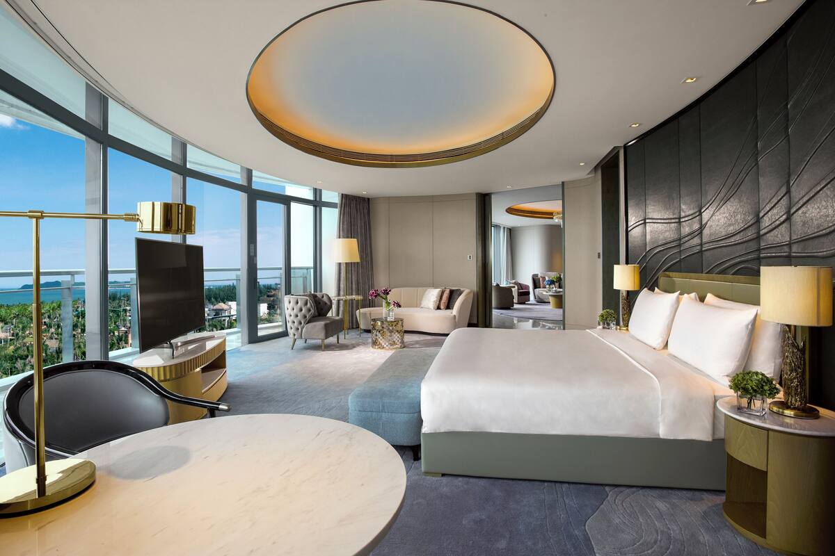 Quarto de hotel moderno com uma cama grande, uma escrivaninha e vista para o oceano.