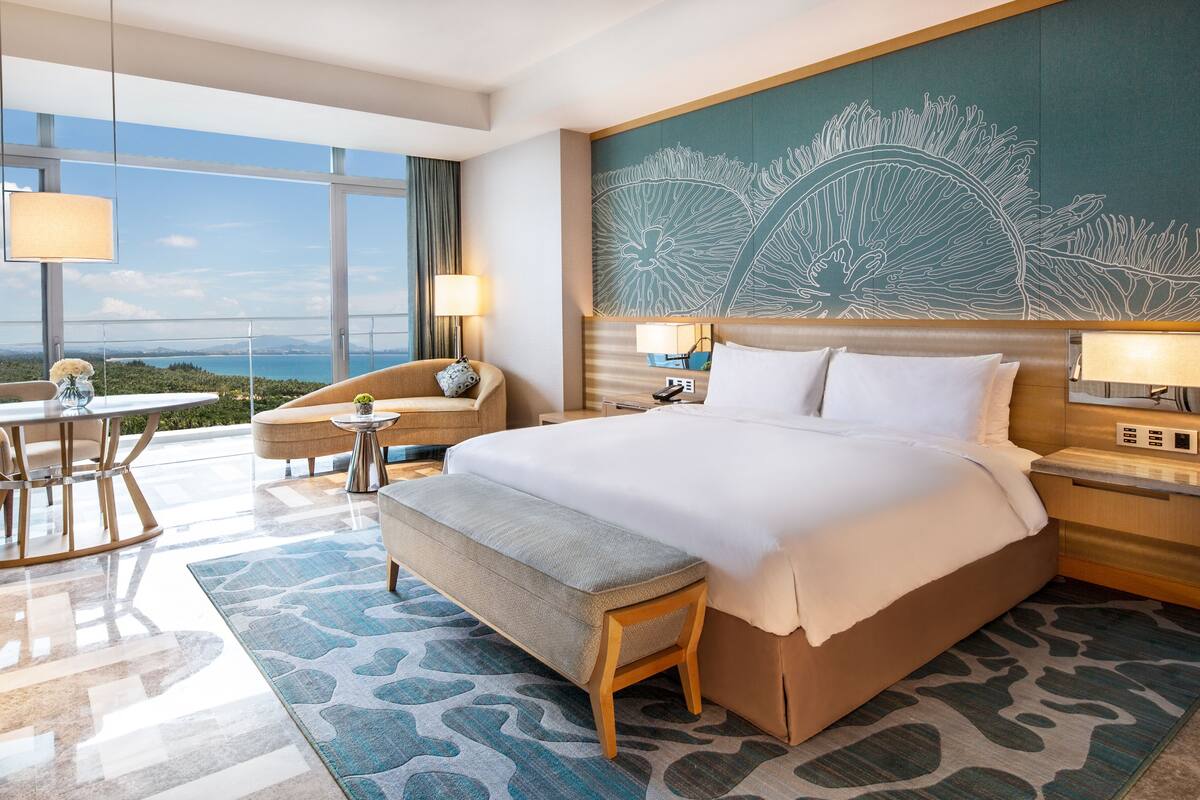 Quarto de hotel moderno com uma cama grande, área de estar com vista e um mural decorativo na parede.
