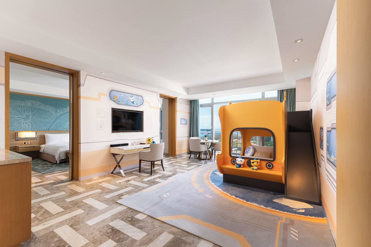 Quarto de hotel moderno com uma janela ampla, um sofá, uma escrivaninha e uma televisão.