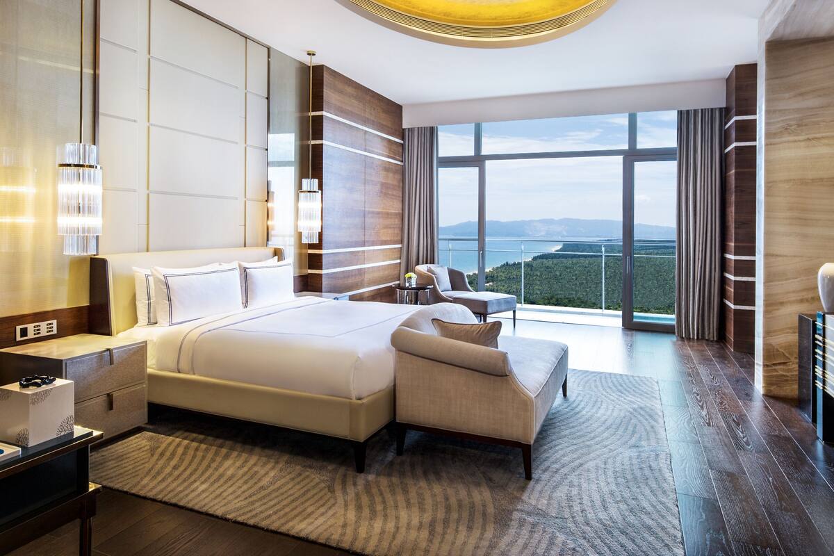 Quarto de hotel moderno com uma cama grande, um espaço de estar e vista para as montanhas.