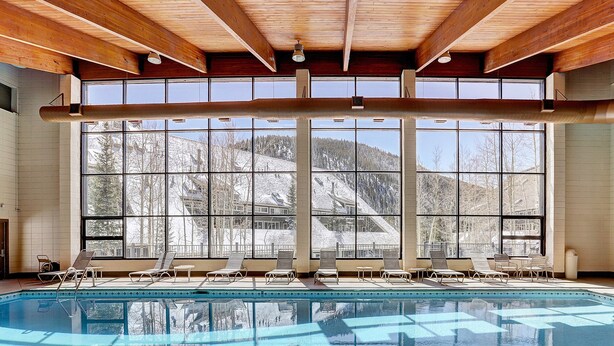 Uma grande piscina interna com vista para montanhas cobertas de neve através de amplas janelas.