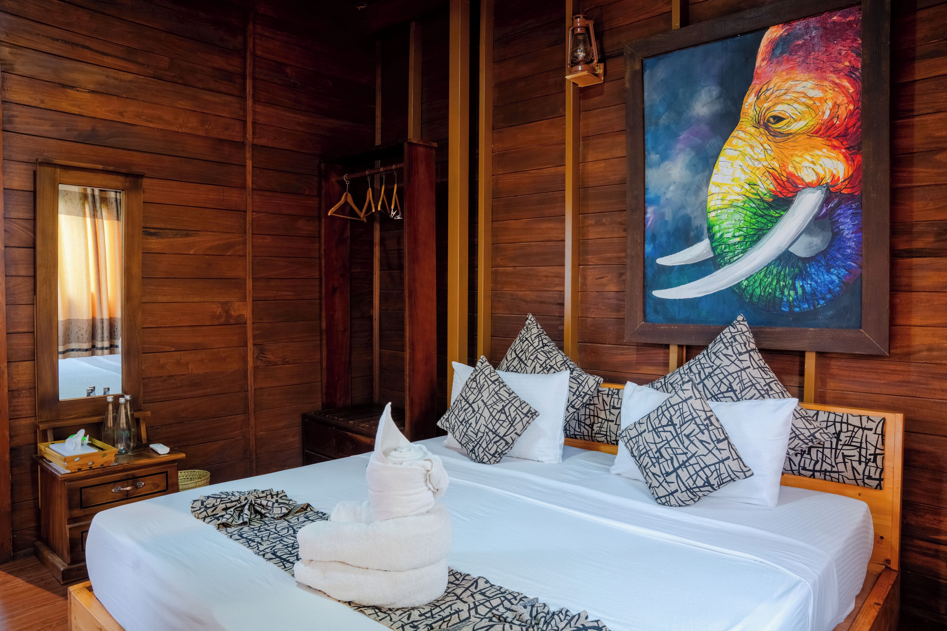 Quarto de madeira com uma cama, almofadas, pintura de um elefante e luminária pendente.