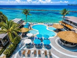 Área de piscina do resort, com várias piscinas, espreguiçadeiras, guarda-sóis e vista para o oceano.