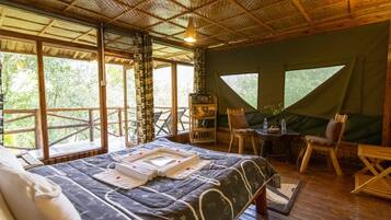 Quarto amplo com uma cama grande, uma mesa pequena com cadeiras e vista para o exterior através de grandes janelas.