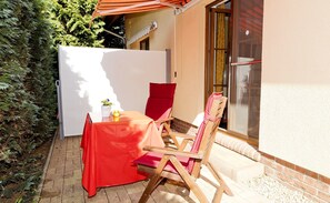Um pátio com mesa e cadeiras, uma divisória branca e um muro de tijolos.