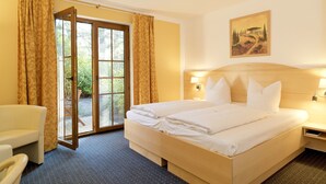 Quarto de hotel com cama de casal, uma cadeira, escrivaninha com luminária e um quadro na parede.