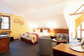 Quarto de hotel com cama, escrivaninha, cadeira, mesinha e janela.