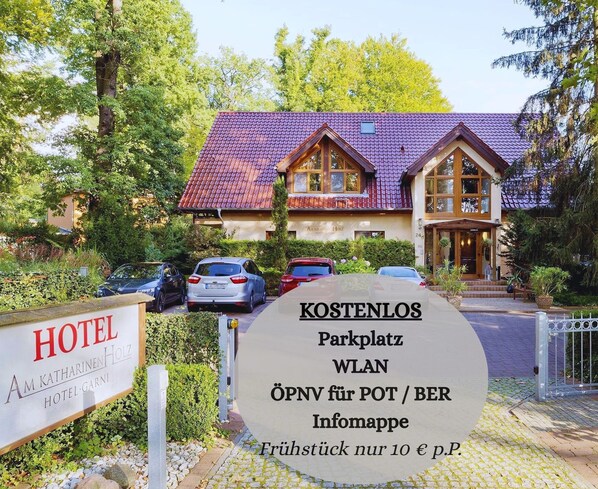 Um hotel com uma placa indicando 'HOTEL AM KATHARINENHOLZ HOTEL-GARNI' e uma área de estacionamento com uma placa informando 'KOSTENLOS Parkplatz WLAN ÖPNV para POT / BER Infoapppe Pequeno-almoço apenas 10 € por pessoa'.