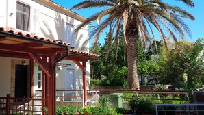 Uma casa com varanda, uma palmeira e um jardim com diversas plantas e flores.