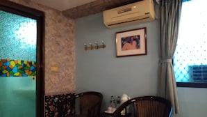 Quarto com parede de pedra, um quadro emoldurado, aparelho de ar condicionado e duas cadeiras de madeira.