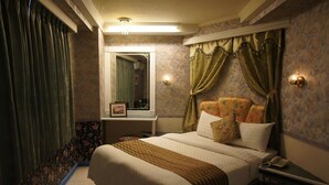 Quarto de hotel com cama, mesa de cabeceira com telefone, espelho e cortinas.
