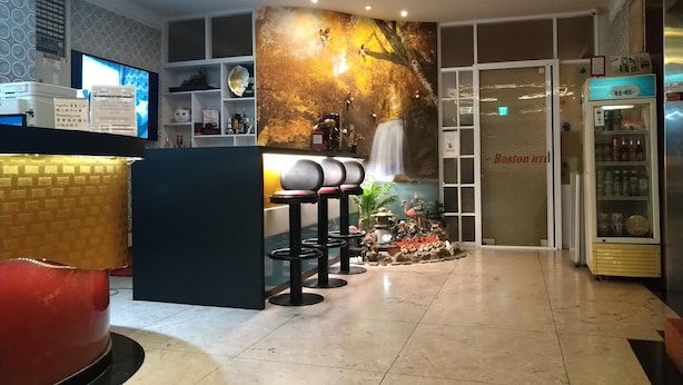 Uma área de recepção de hotel com balcão, assentos, parede decorativa e um refrigerador.