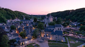Vista aérea de uma cidade histórica com um castelo imponente, ruas de paralelepípedos e vegetação ao redor.