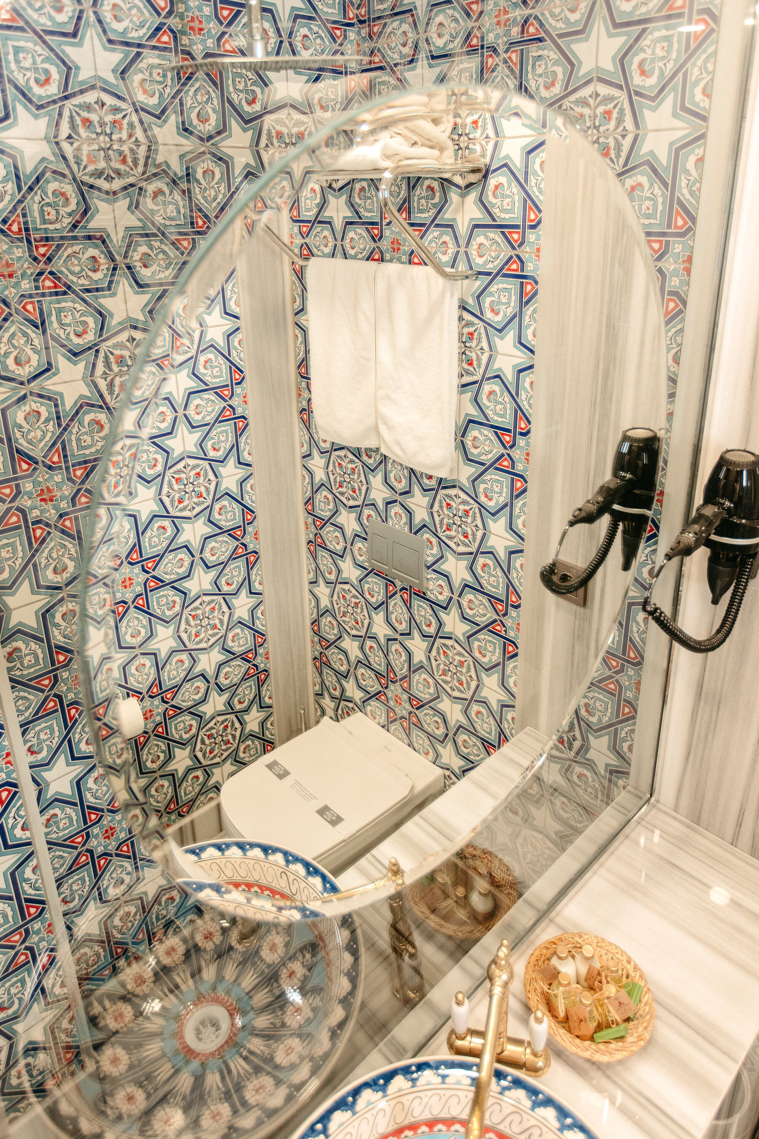 Um banheiro com azulejos estampados, box de vidro, porta-toalhas e toucador com um prato decorativo.