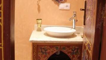 Um banheiro com pia branca, espelho e um armário decorativo.