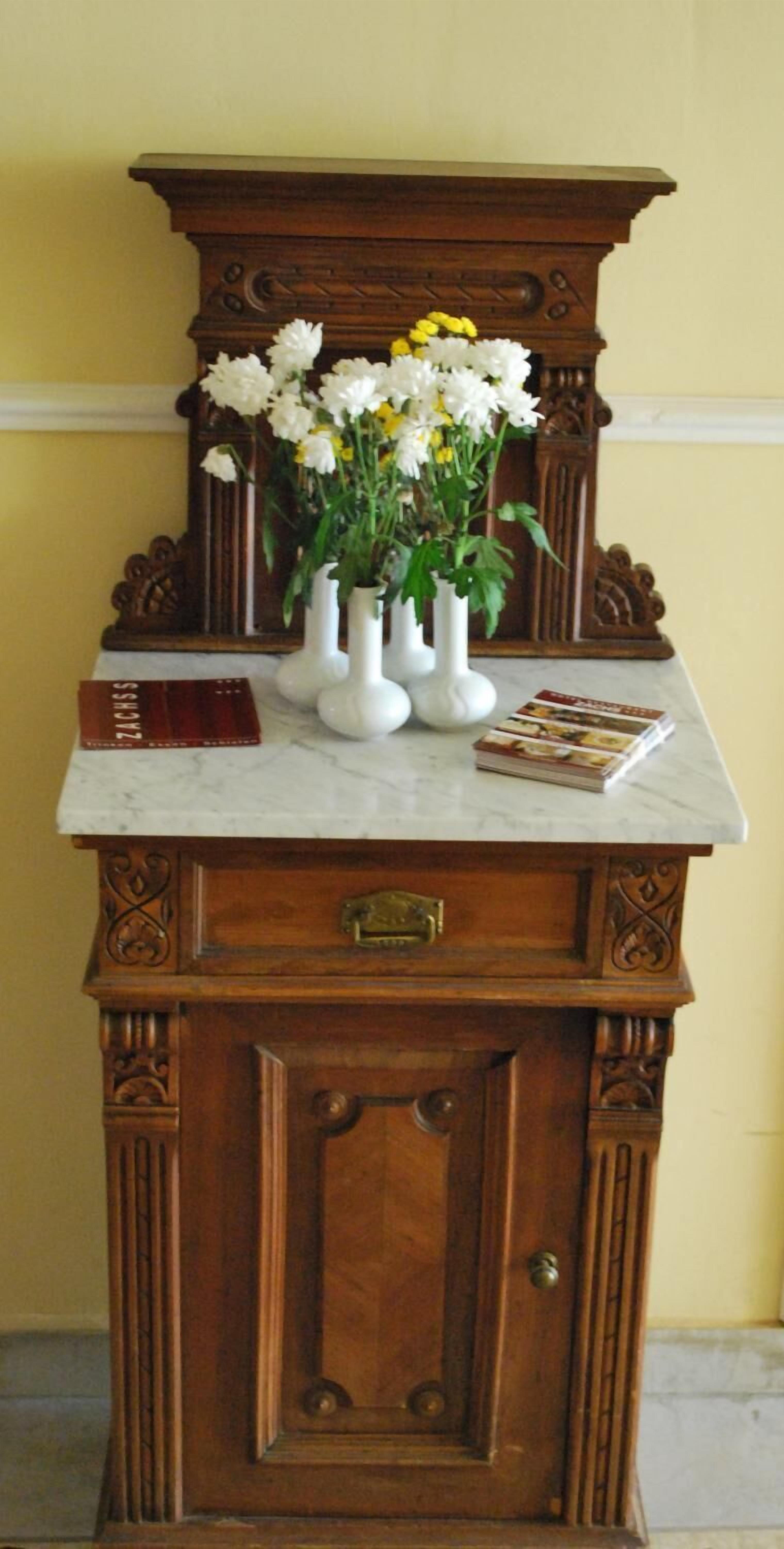 Um armário de madeira com bancada de mármore, contendo um vaso com flores e um livro.