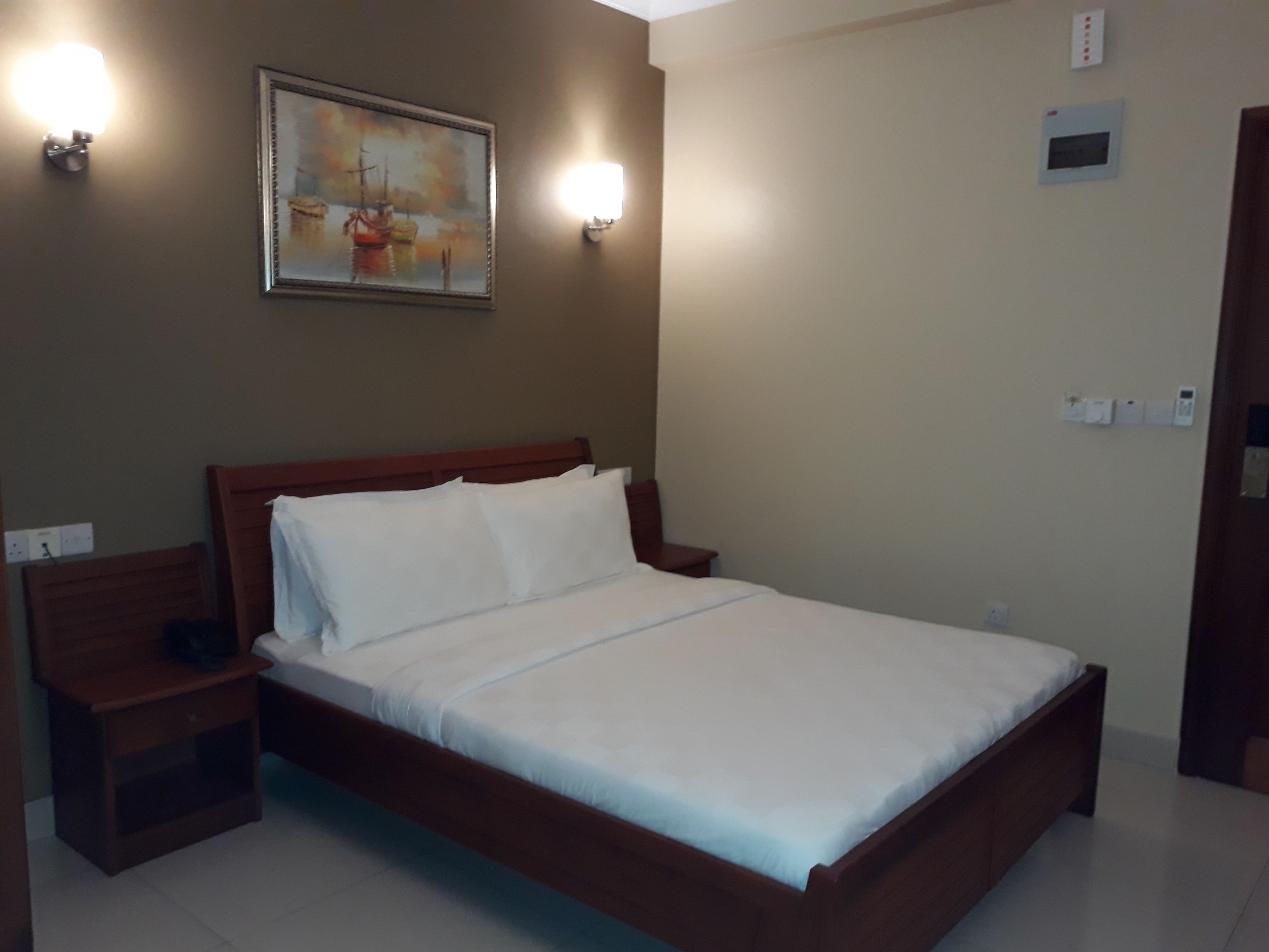 Uma cama bem arrumada em quarto de hotel, com cabeceira de madeira, duas mesas de cabeceira e um quadro pendurado na parede.