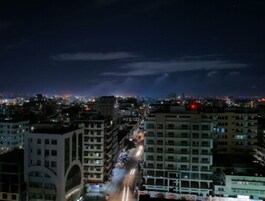 Paisagem urbana noturna com edifícios e uma rua movimentada.