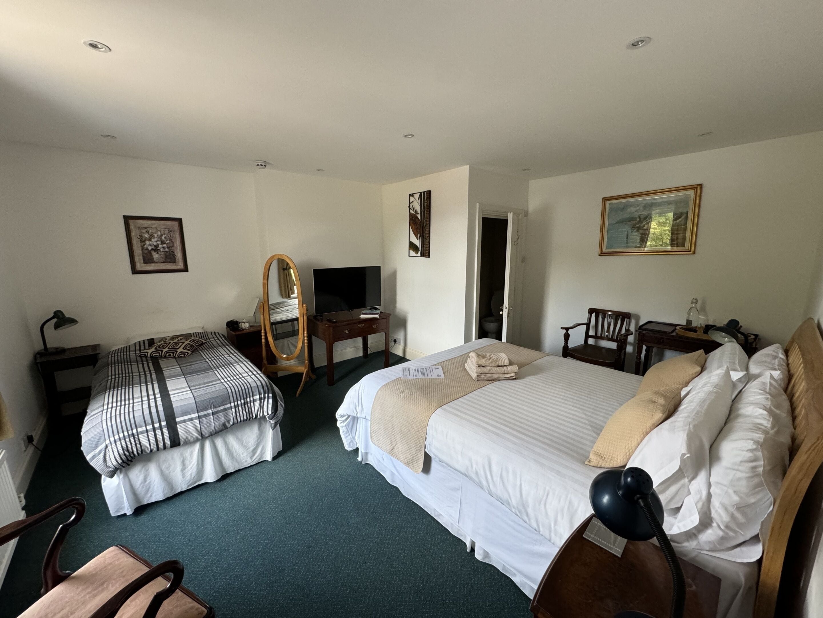 Quarto de hotel com duas camas, uma mesa com computador, uma cadeira, um espelho e um telefone.