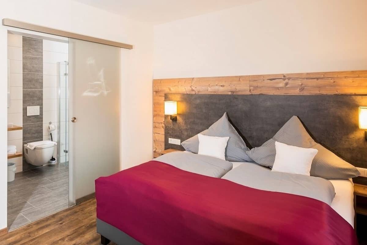 Quarto de hotel com uma cama, cabeceira de madeira e mesa de cabeceira com abajur.