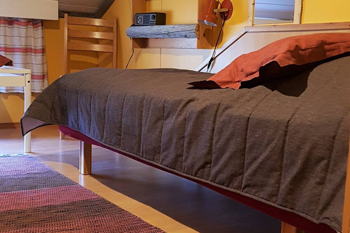Quarto estilo dormitório com beliche, escrivaninha pequena, cadeira, rádio e janela com persianas.