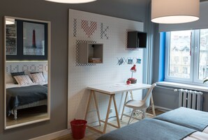 Quarto com cama, escrivaninha e cadeira. Janela com vista para prédios.