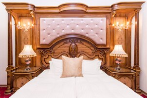 Uma cama luxuosa com cabeceira estofada, duas mesas de cabeceira com abajures e um espelho decorativo.