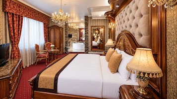 Quarto de hotel com uma cama grande, área de estar com uma poltrona e mesa, televisão e banheiro com espelho e pia.