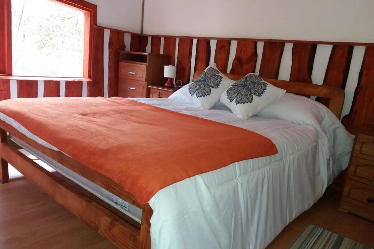 Uma cama com cabeceira de madeira, roupa de cama branca e almofadas decorativas.