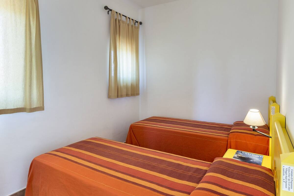 Quarto com duas camas, uma luminária pendente e uma janela com cortinas.