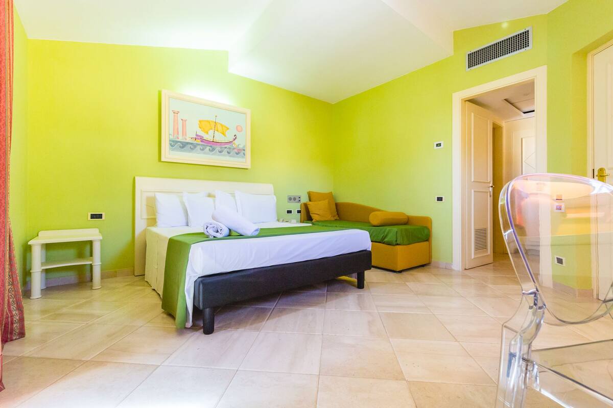 Quarto com uma cama, mesa de cabeceira, uma cadeira e um quadro na parede.