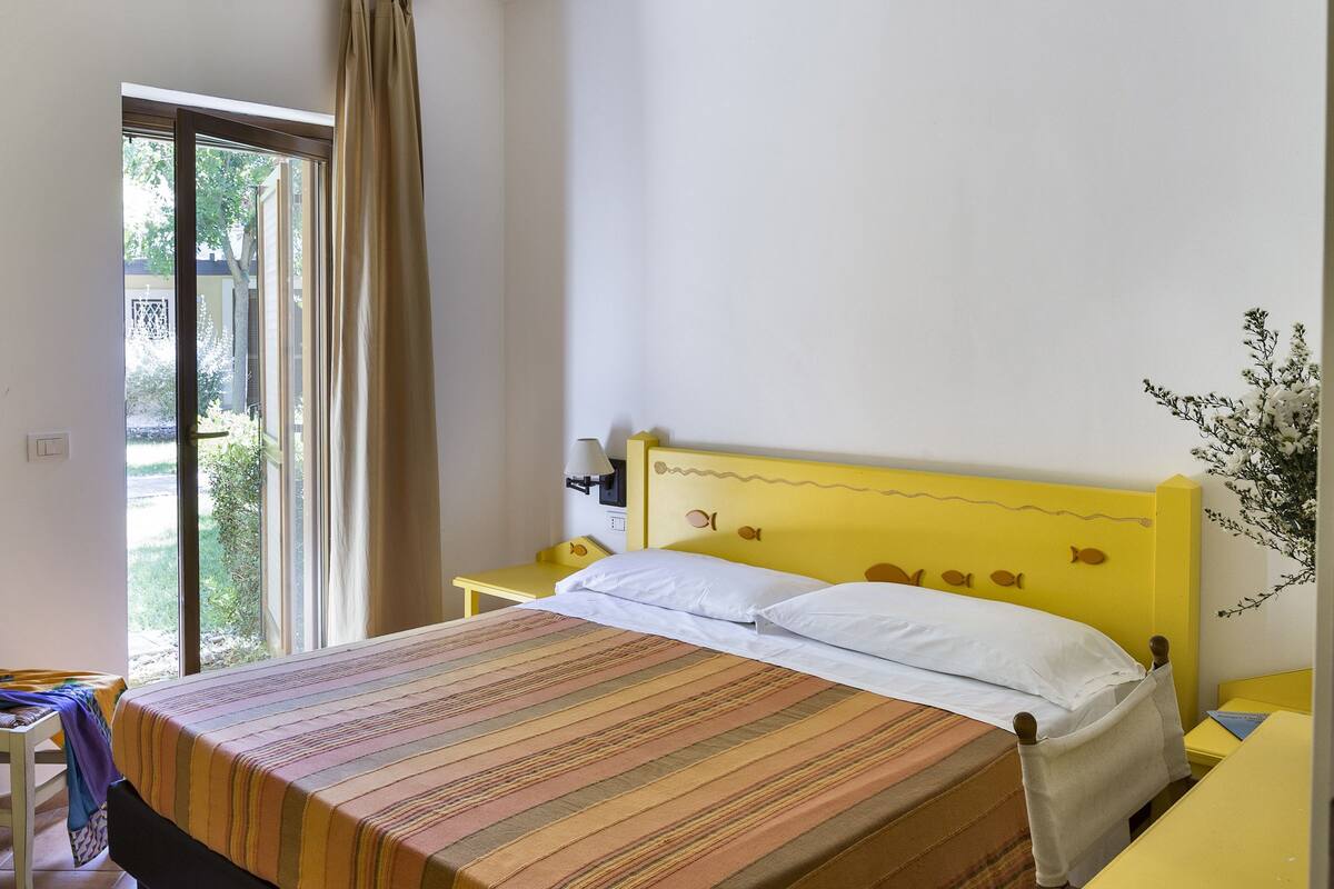 Uma cama com colcha listrada, cabeceira amarela e almofadas brancas.