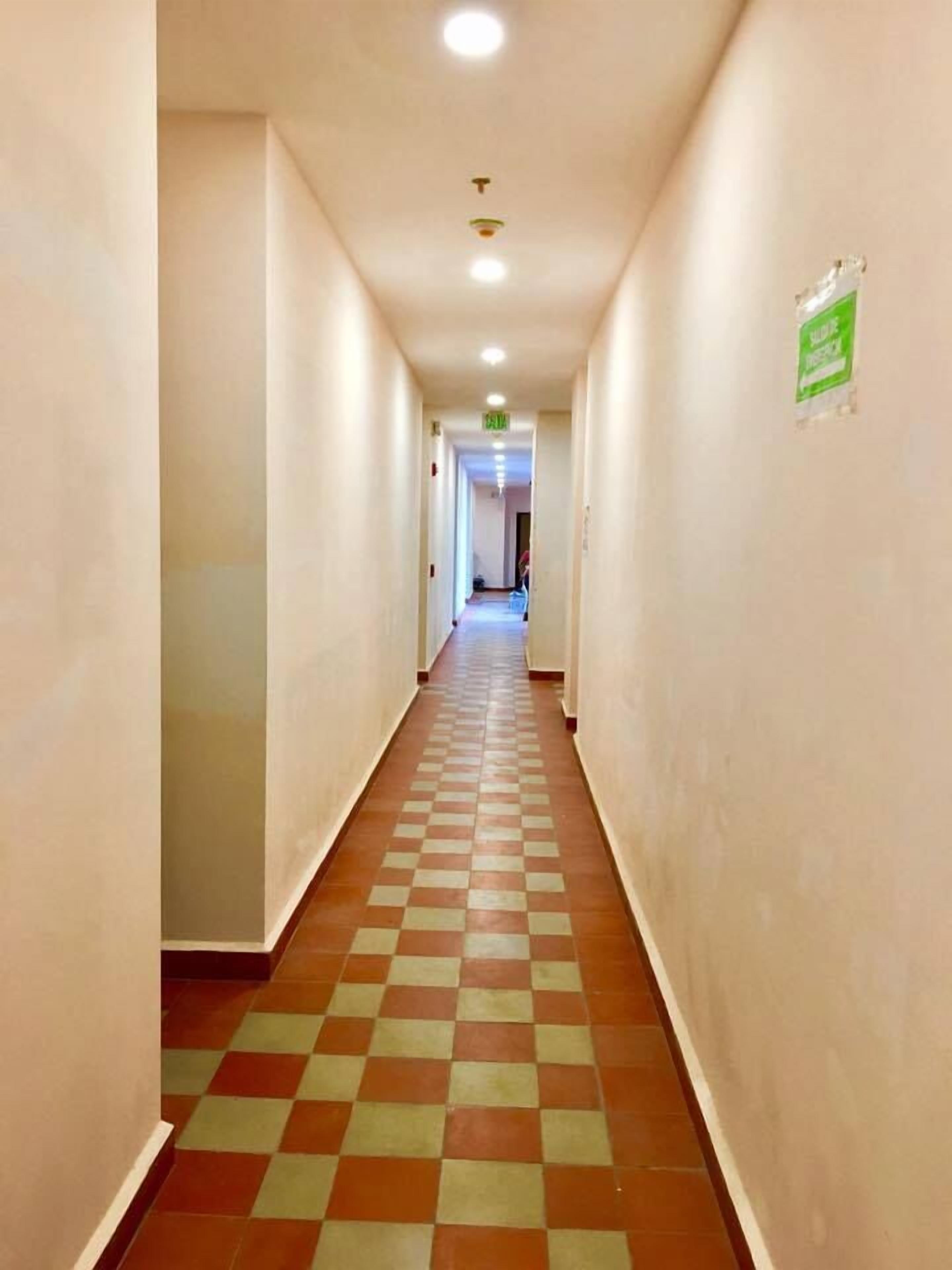 Um corredor comprido e estreito com chão quadriculado e paredes brancas.