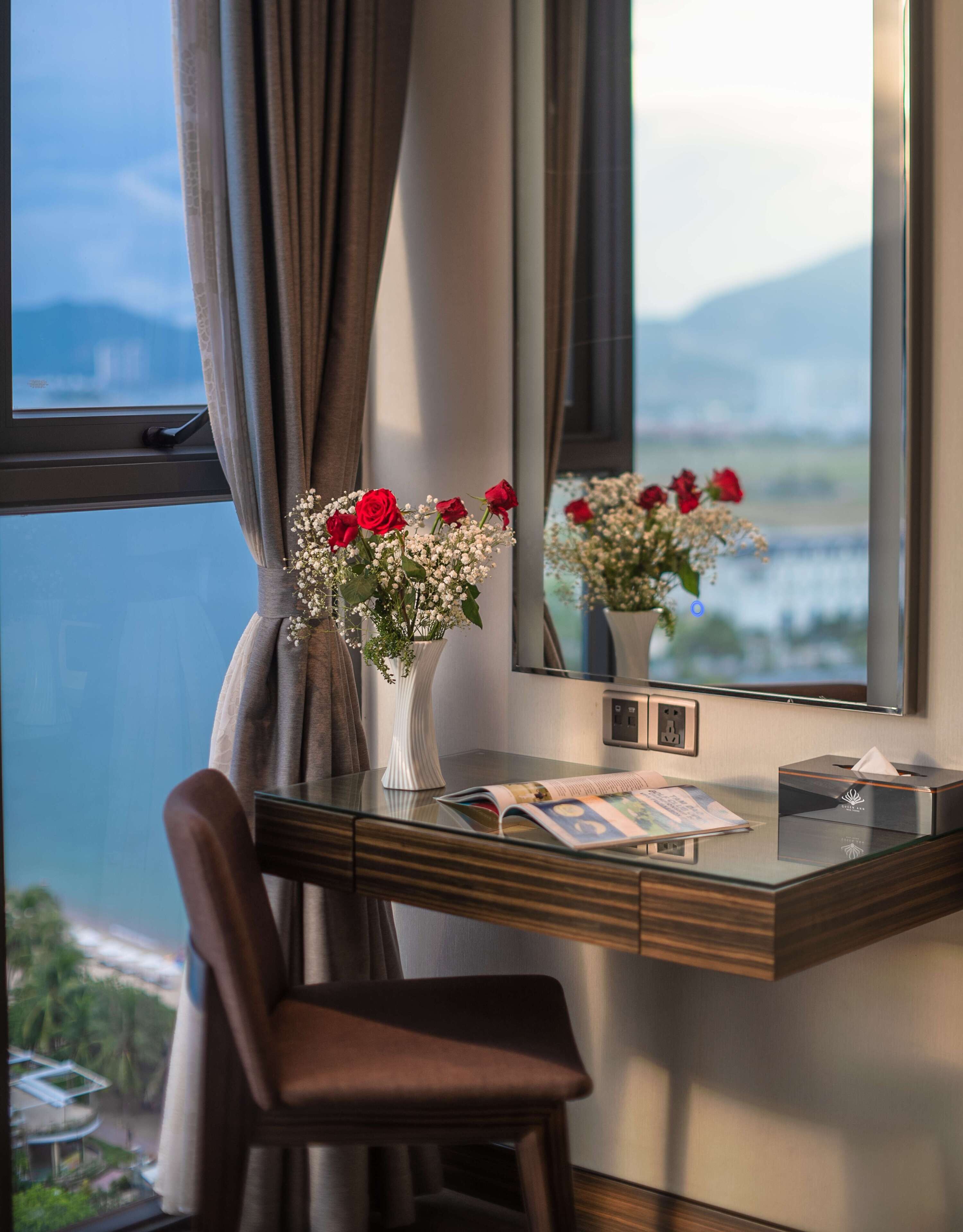 Quarto de hotel moderno com escrivaninha, cadeira e um vaso de rosas vermelhas.