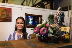 Uma área de recepção com uma estátua de Buda, um vaso de flores e uma placa indicando um restaurante.