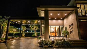 Uma entrada de hotel moderna com galeria coberta, portas de vidro e um letreiro que diz 'Dine Your Stay'.
