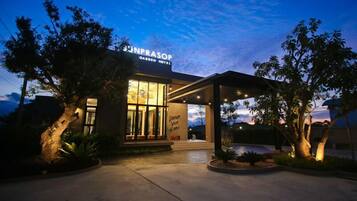 Exterior do JunPrasop Garden Hotel com design moderno, amplas janelas de vidro e área de entrada coberta.
