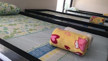 Um quarto de dormitório com beliches, cada um com um edredom colorido e uma toalha enrolada na cama inferior.
