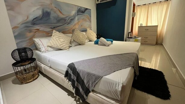 Quarto com cama, ar-condicionado na parede, mesa de cabeceira, luminária e um quadro.